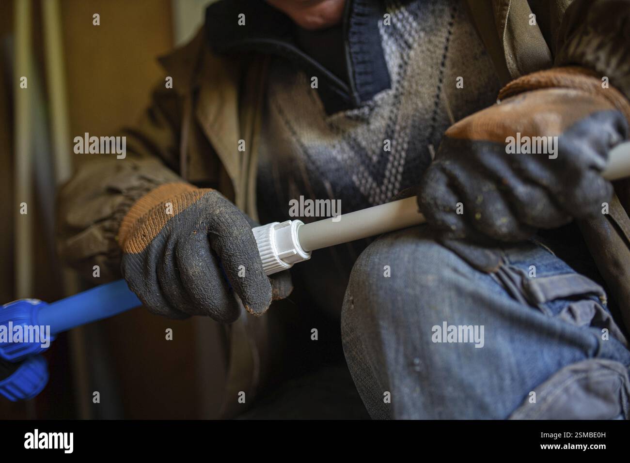 A worker wearing gloves repairing a pipe indoors with a fitting tool ...