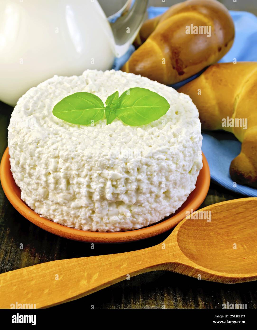 Curd in pottery with basil, wooden spoon, two bagels, a pitcher of milk ...