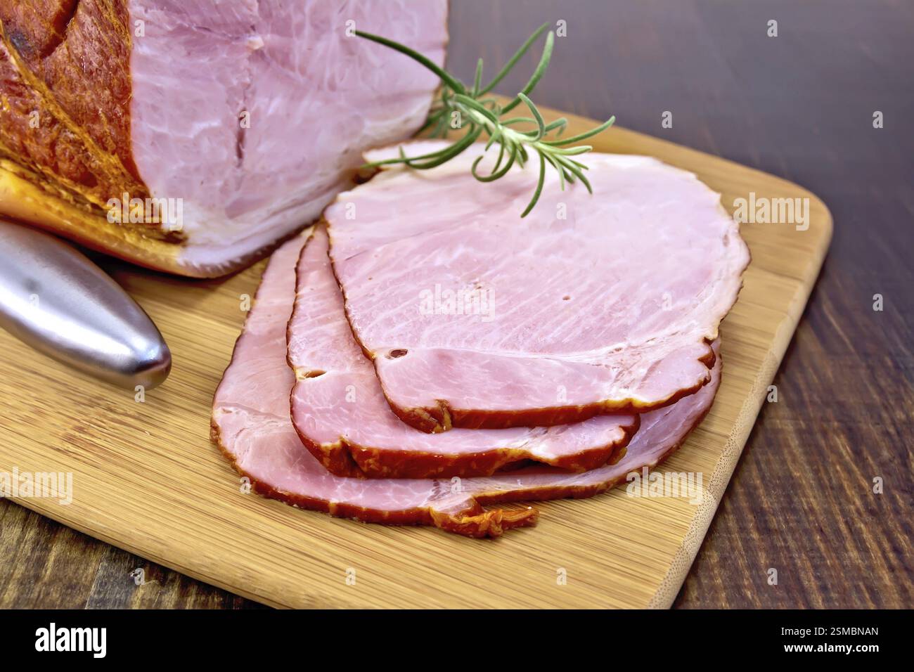Smoked ham, slices of ham with a sprig of rosemary and dark wooden ...