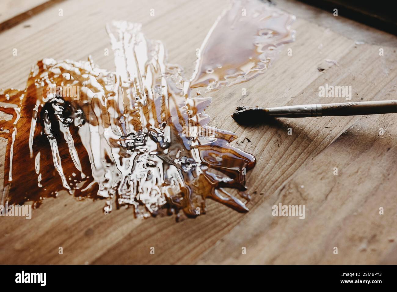 Wooden surface with varnish spill and a paintbrush, creating a smooth ...