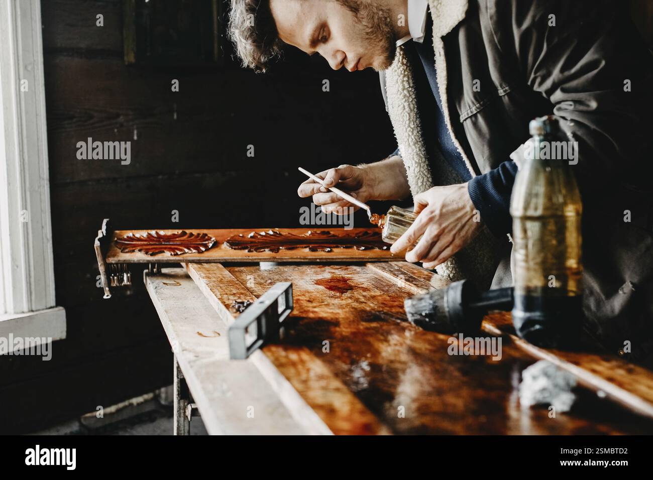 Man immersed in detailed woodwork, using tools to apply finish to wood ...