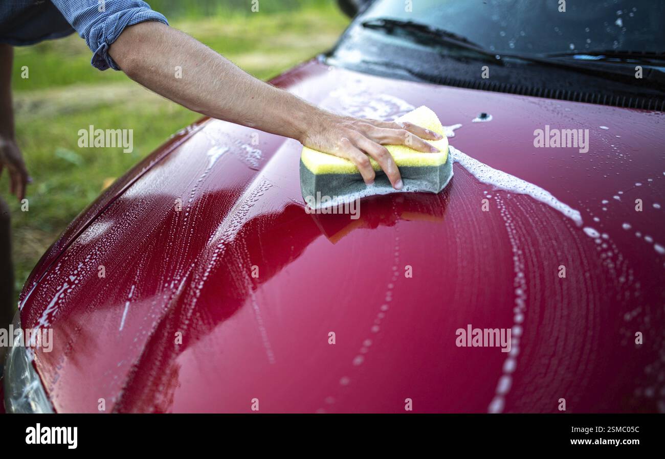 Close-up of a hand washing the hood of a red car with a sponge and soap ...