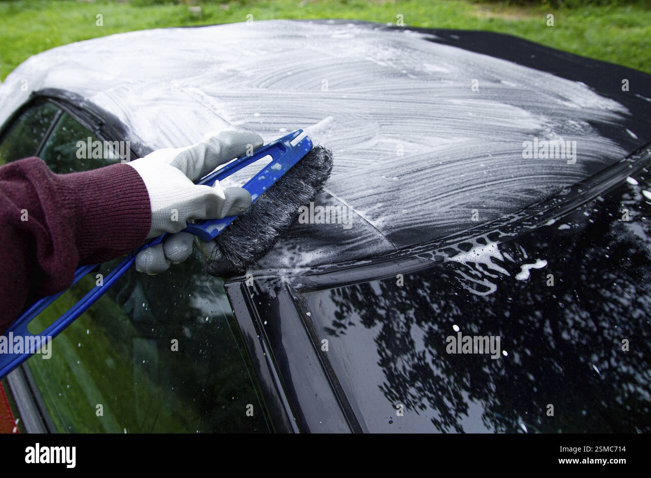 A person cleaning a car's rooftop with a brush and soap in an outdoor ...