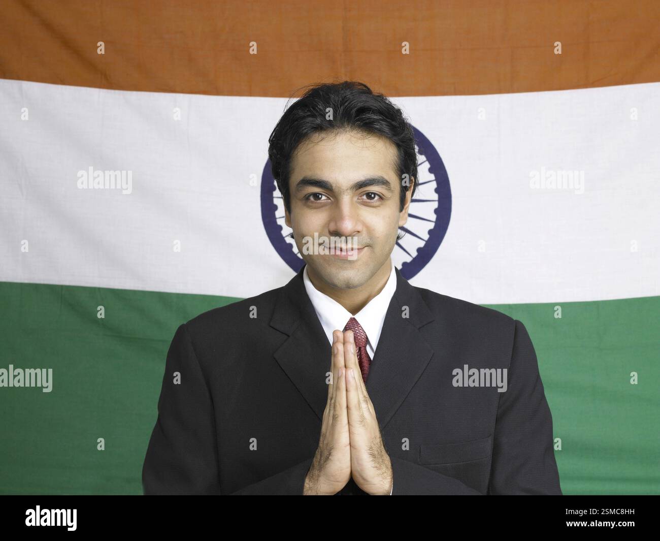 South Asian Indian executive in welcome pose standing in front of flag ...