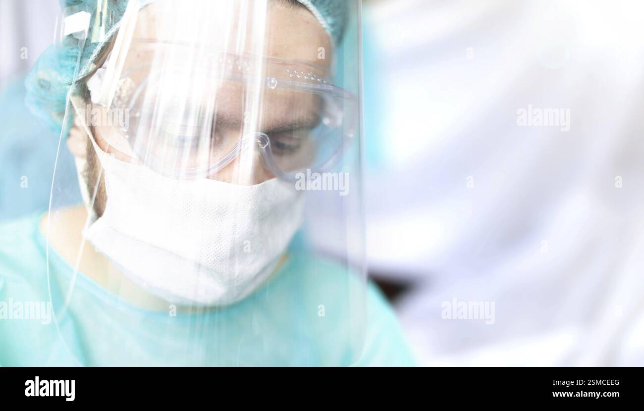 Medical operative wearing a face shield, mask and goggles, focused ...
