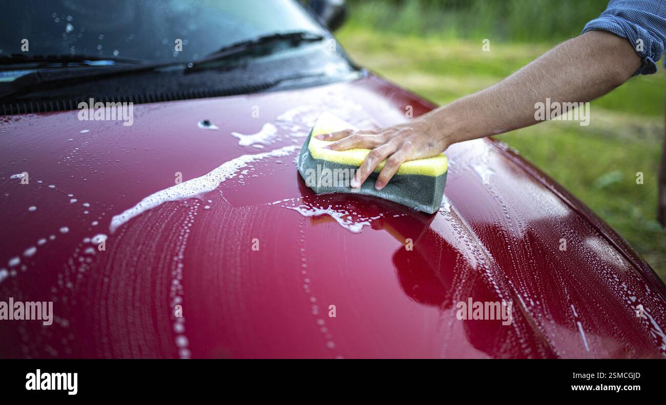 A hand scrubbing soap on a red car with a sponge, creating suds Stock ...