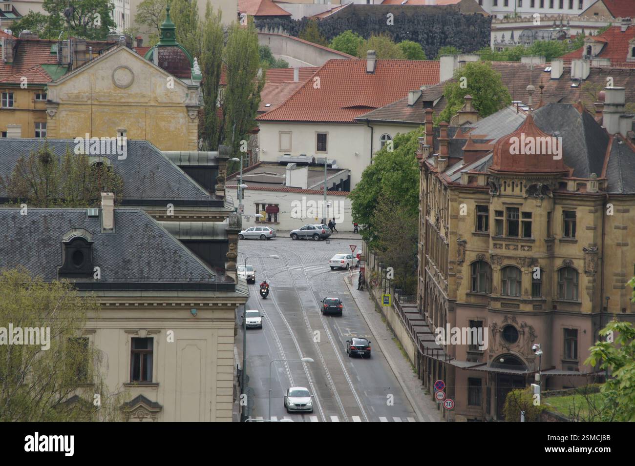 Sloped street in Prague. Historic buildings line the street. Cars and ...