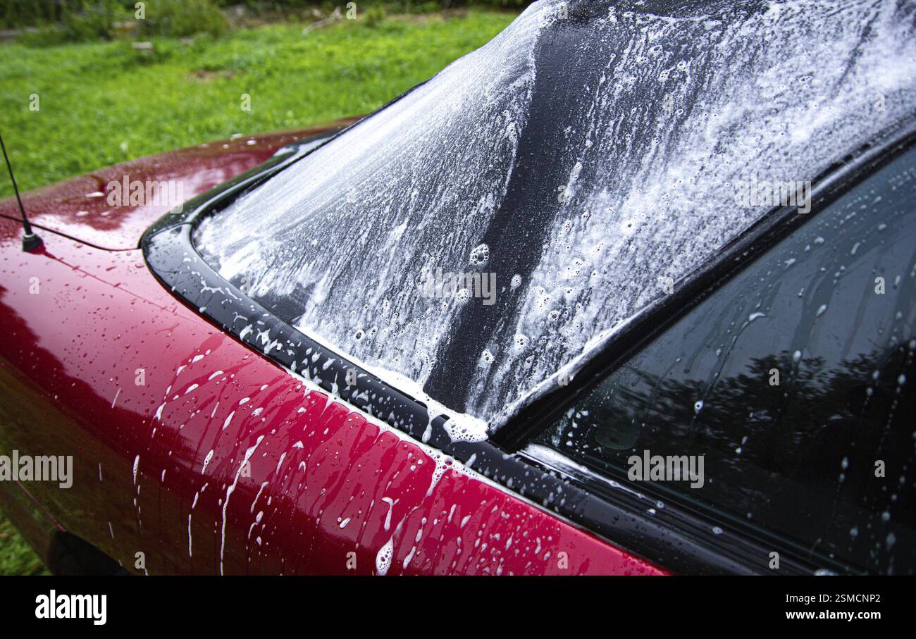 The rear window of a red car covered in soap suds after cleaning ...