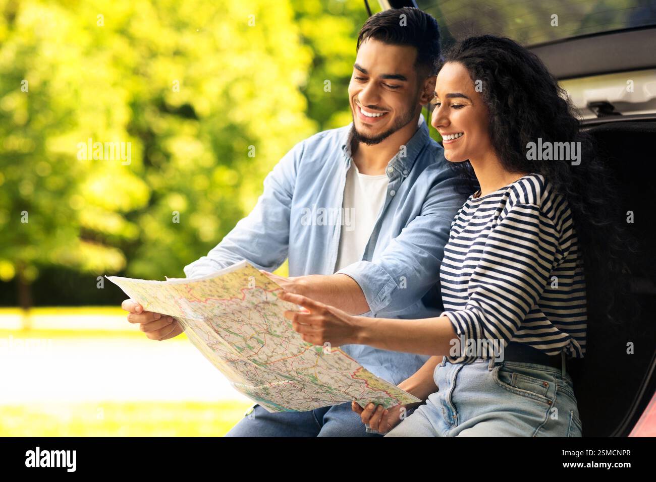 Happy lovers sitting on car trunk and watching map Stock Photo - Alamy