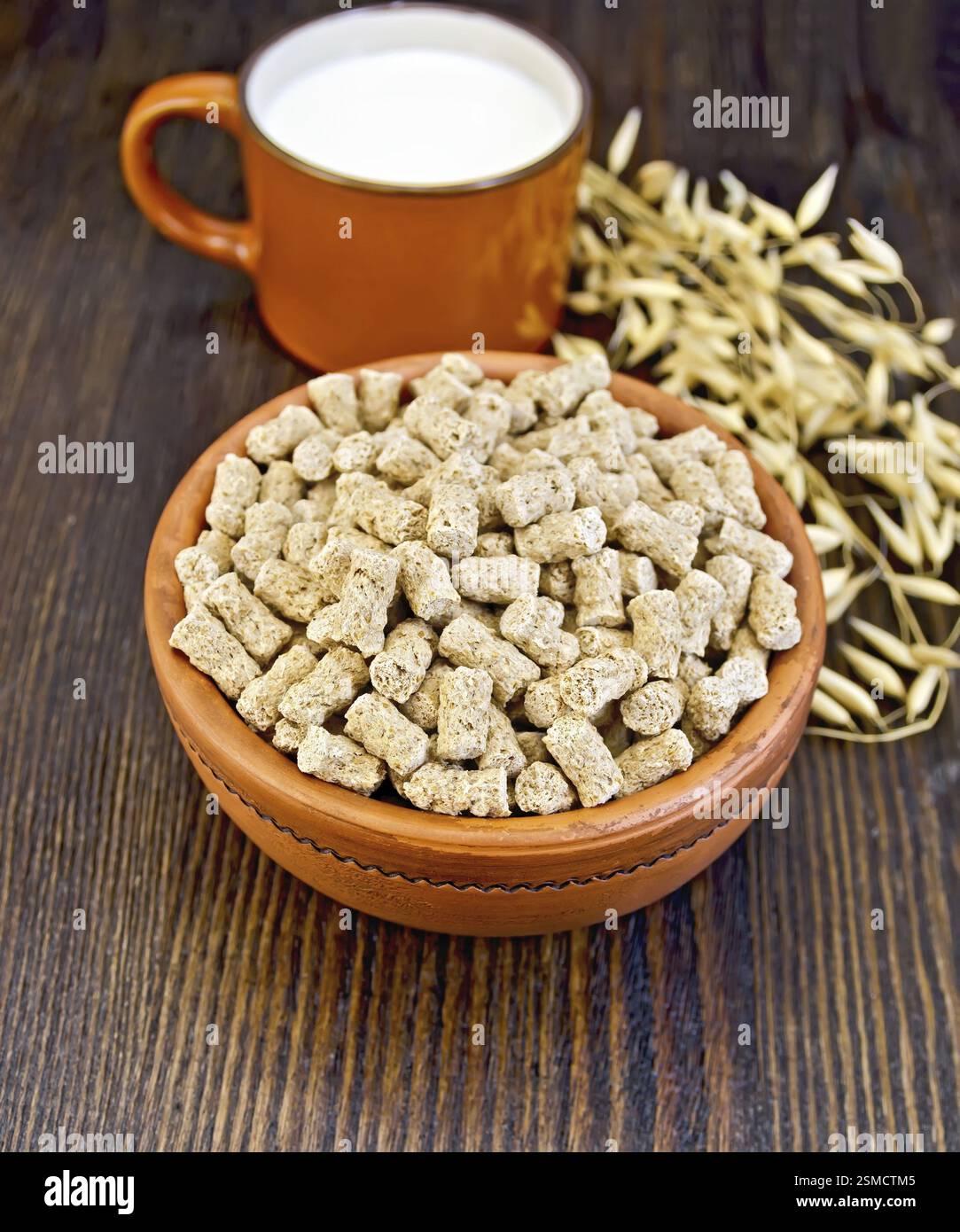 Oat bran large in earthenware bowl, a mug with milk, oat stalks on a ...