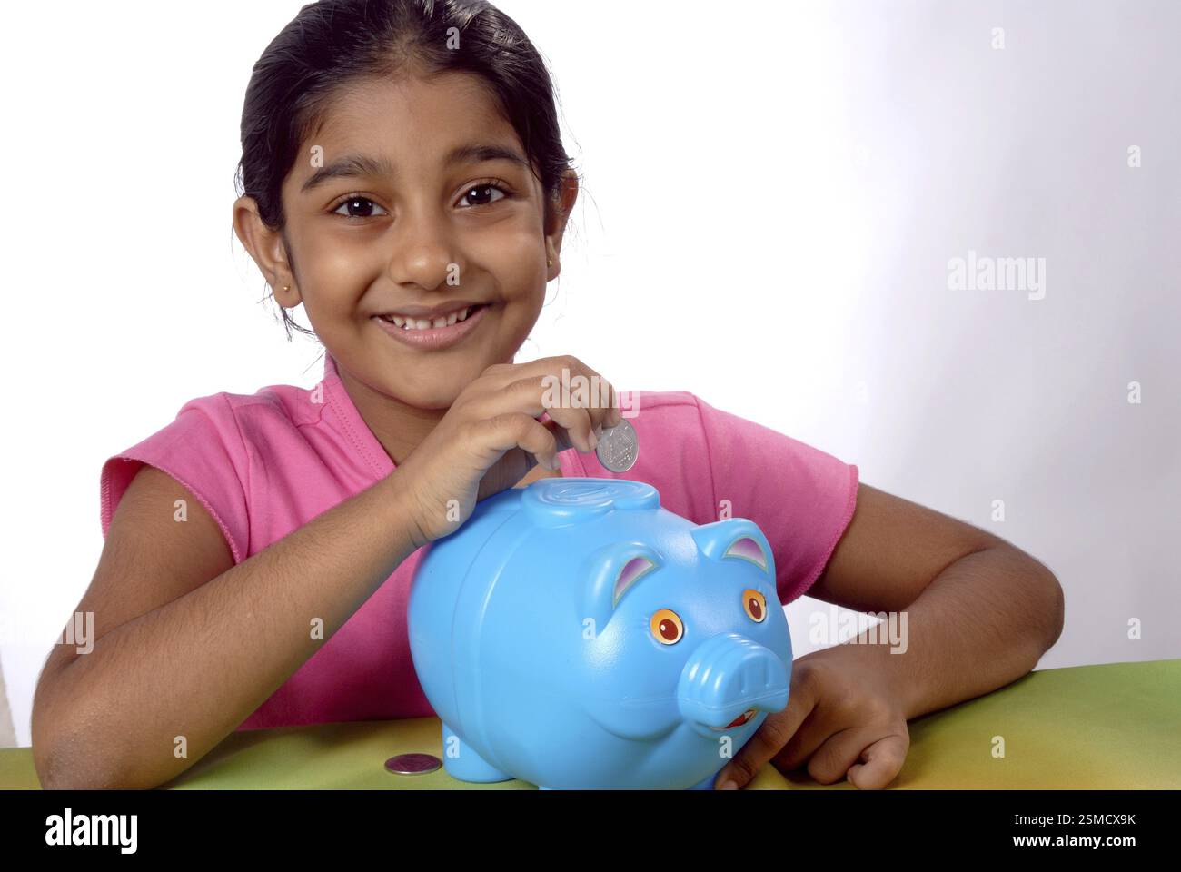 South Asian Indian six year old girl saving coins in piggy bank MR#152 ...
