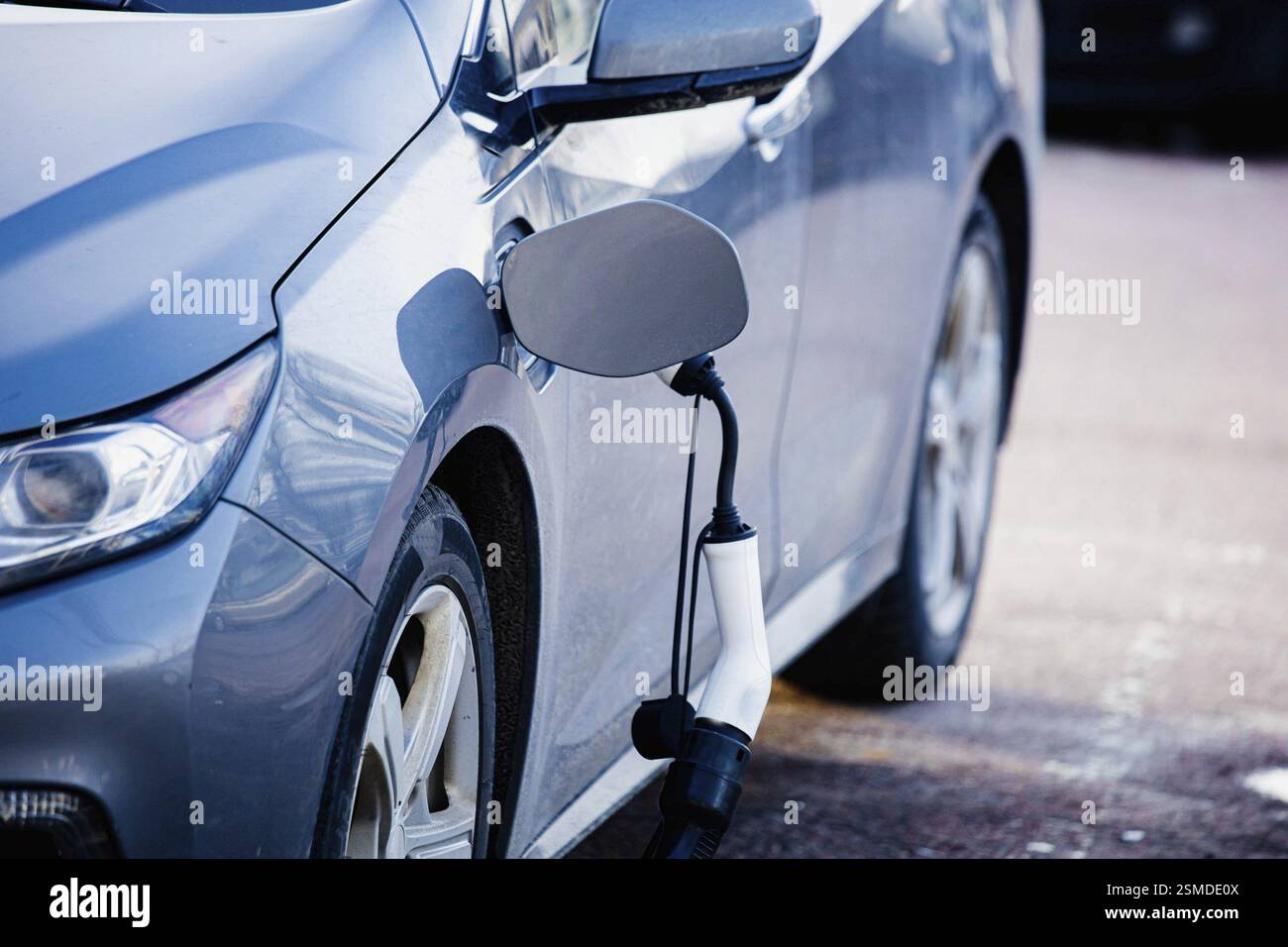 A blue electric car plugged in for charging on a city street Stock ...