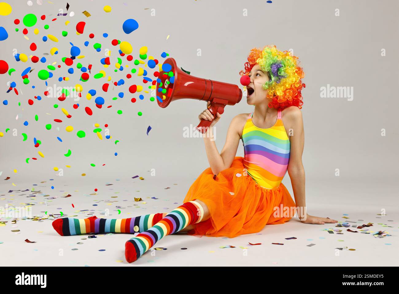 Cute girl dressed like clown shouting in megaphone with confetti flying ...