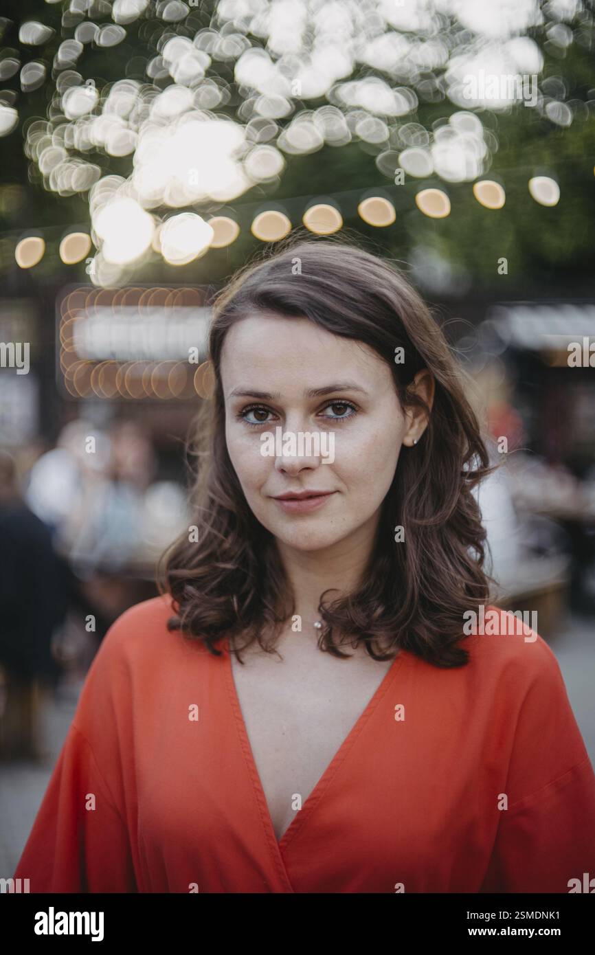 Woman in an orange dress in an outdoor setting with bokeh lights ...