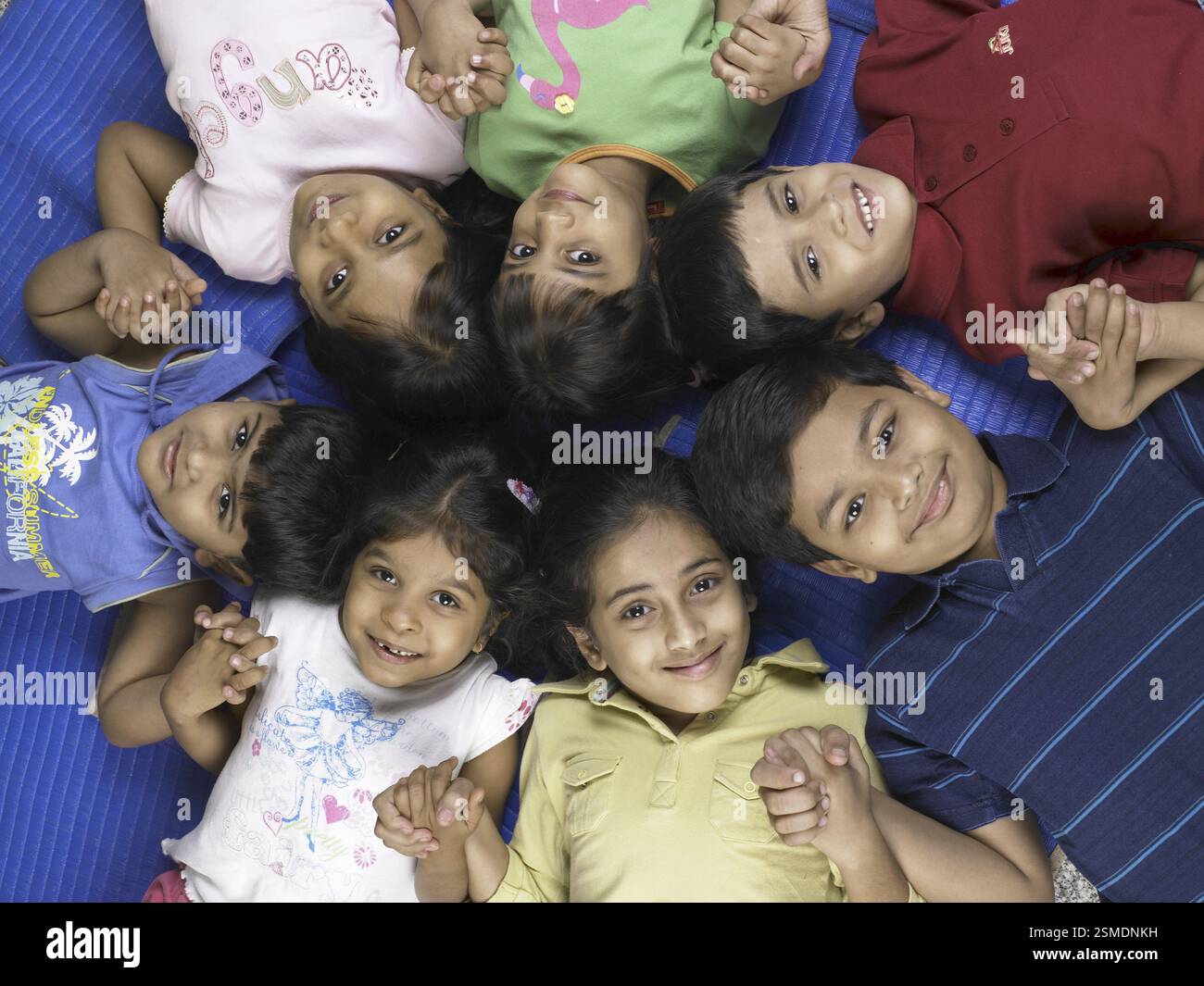 South Asian Indian boys and girls lay down on floor and holding hands ...