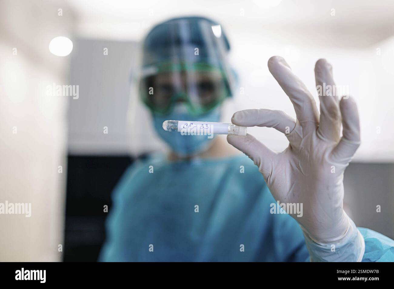 Medical person in protective gear holding a labeled test tube in a ...