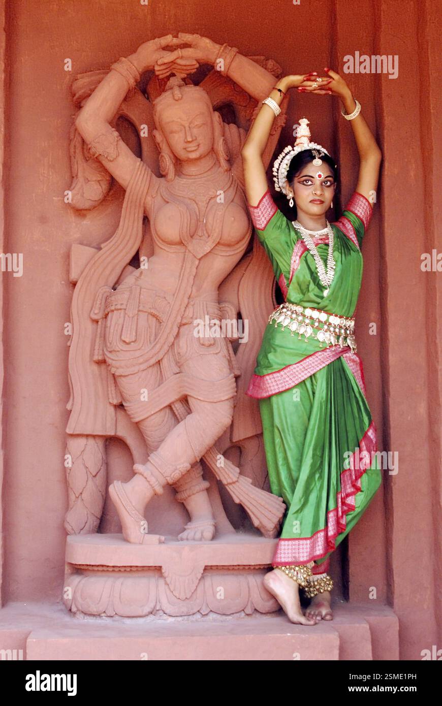 Woman performing classical traditional Odissi dance at statue on stage ...
