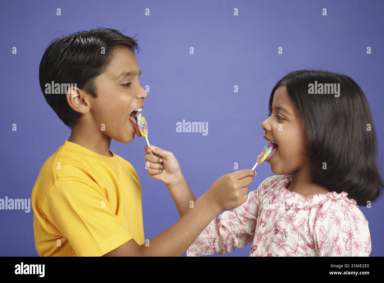 Ten and eight year old boy and girl feeding lollipops to each other MR ...