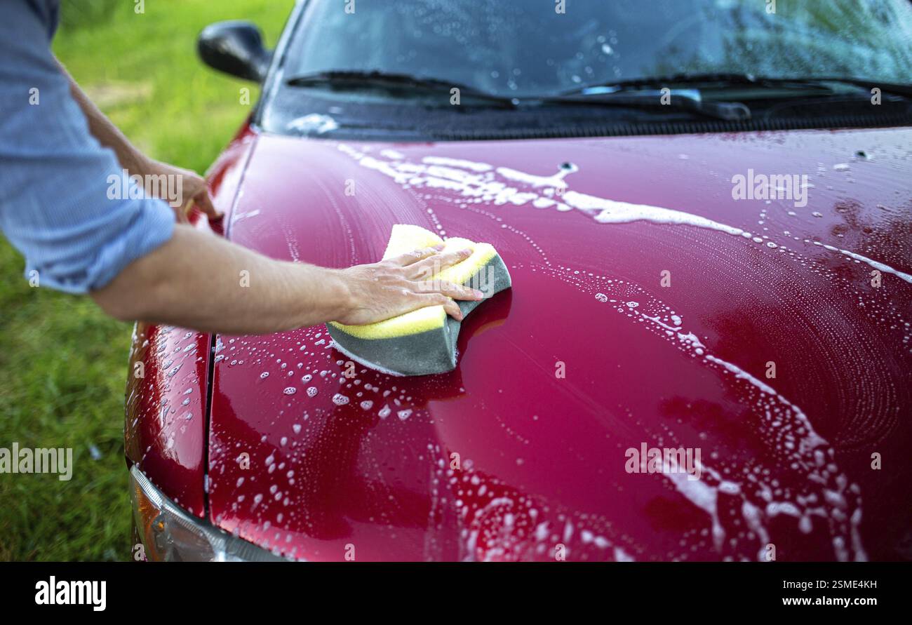 Hand using a sponge to wash the hood of a red car with soap and suds ...