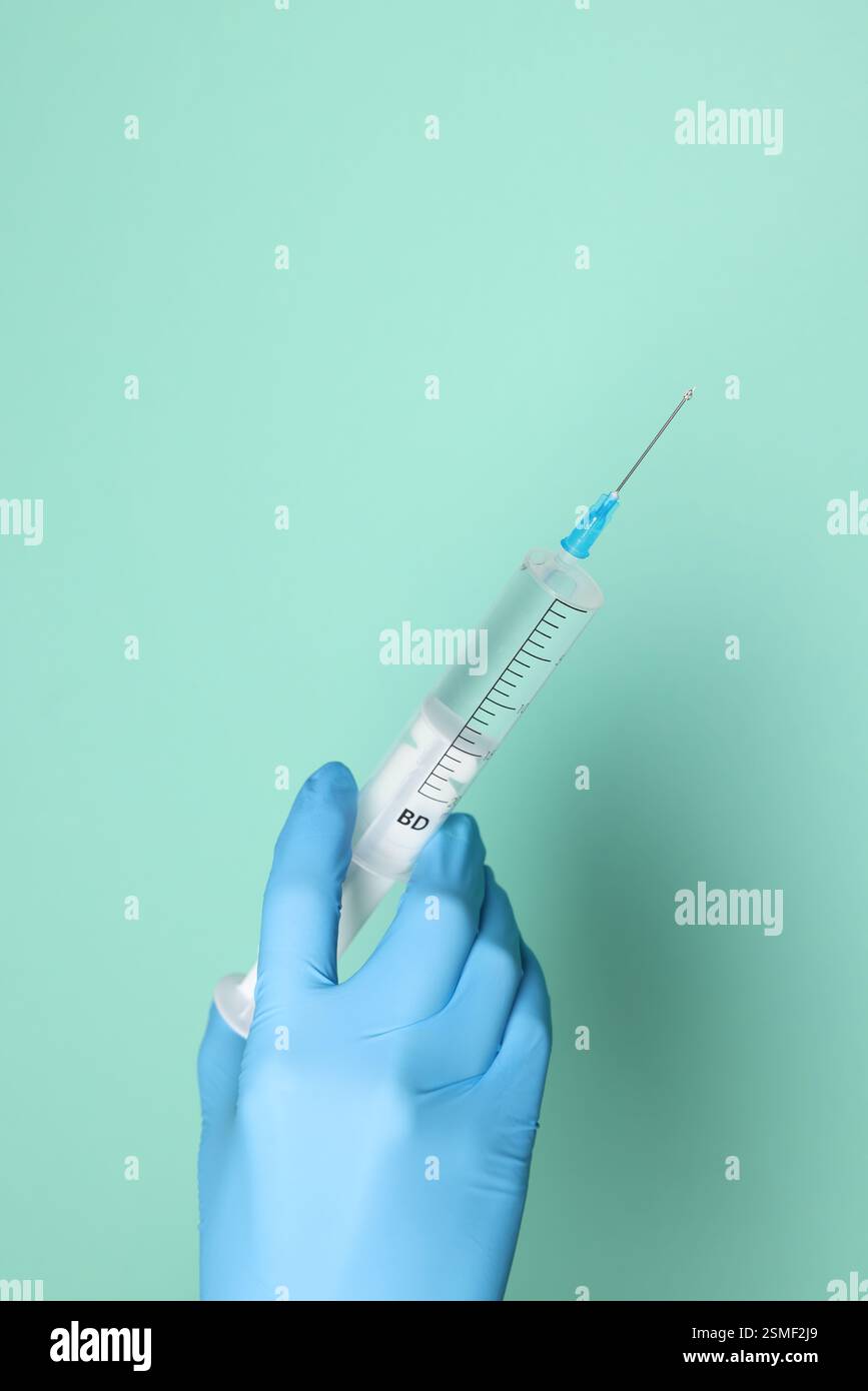 Doctor holding syringe with medication on turquoise background, closeup ...
