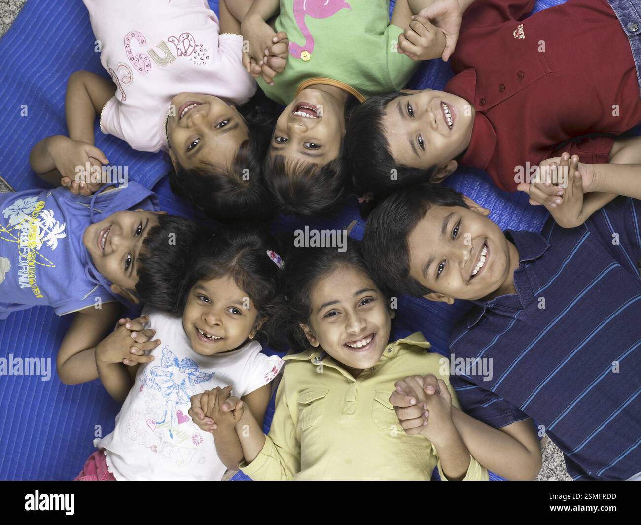 South Asian Indian boys and girls lay down on floor and holding hands ...