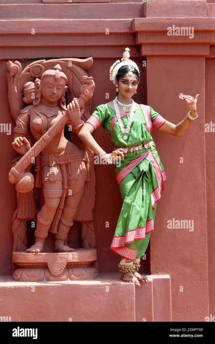 Woman performing classical traditional Odissi dance at statue on stage ...