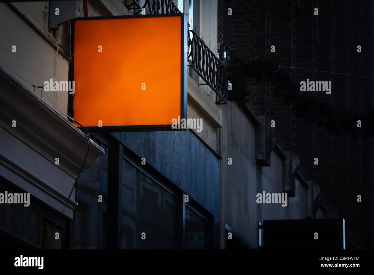 A bright orange sign hangs empty above a shop entrance on a bustling ...