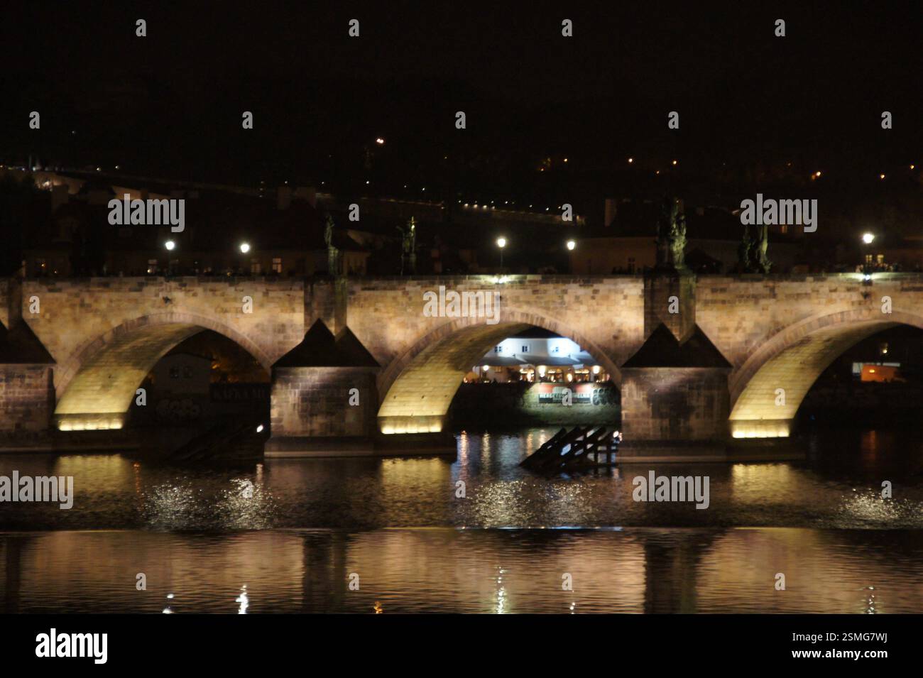 Charles Bridge. Illuminated arches span the Vltava River at night. A bustling pedestrian bridge ...