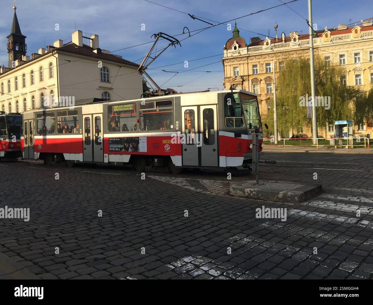 Tram, red and white, driving on cobblestone street, sunny day. Czech ...
