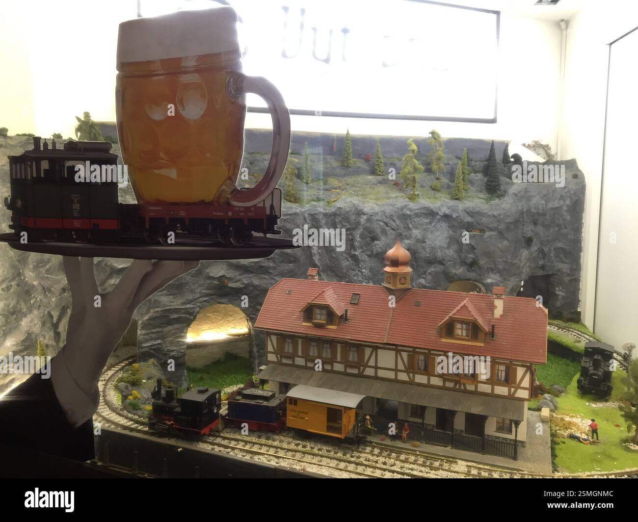 The photo shows a miniature train set and a giant beer mug on a tray ...
