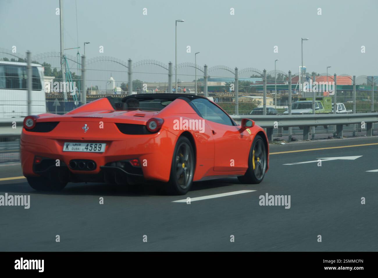 A red Ferrari 458 Spider convertible, top down, cruises a Dubai highway ...