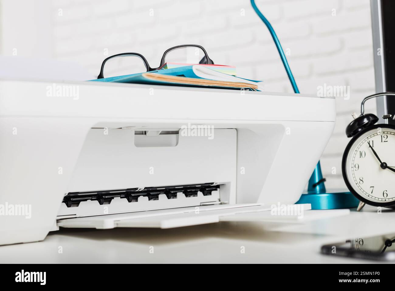 Office workspace with printer, glasses, books, and clock resting on a ...
