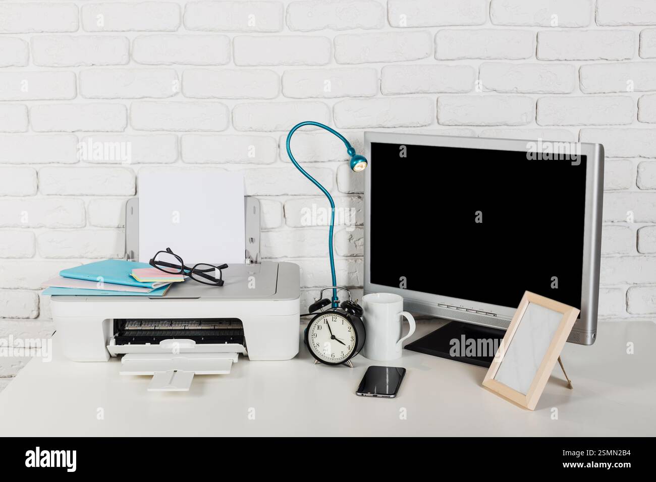 Workspace setup with printer, monitor, clock, and stationery in a ...