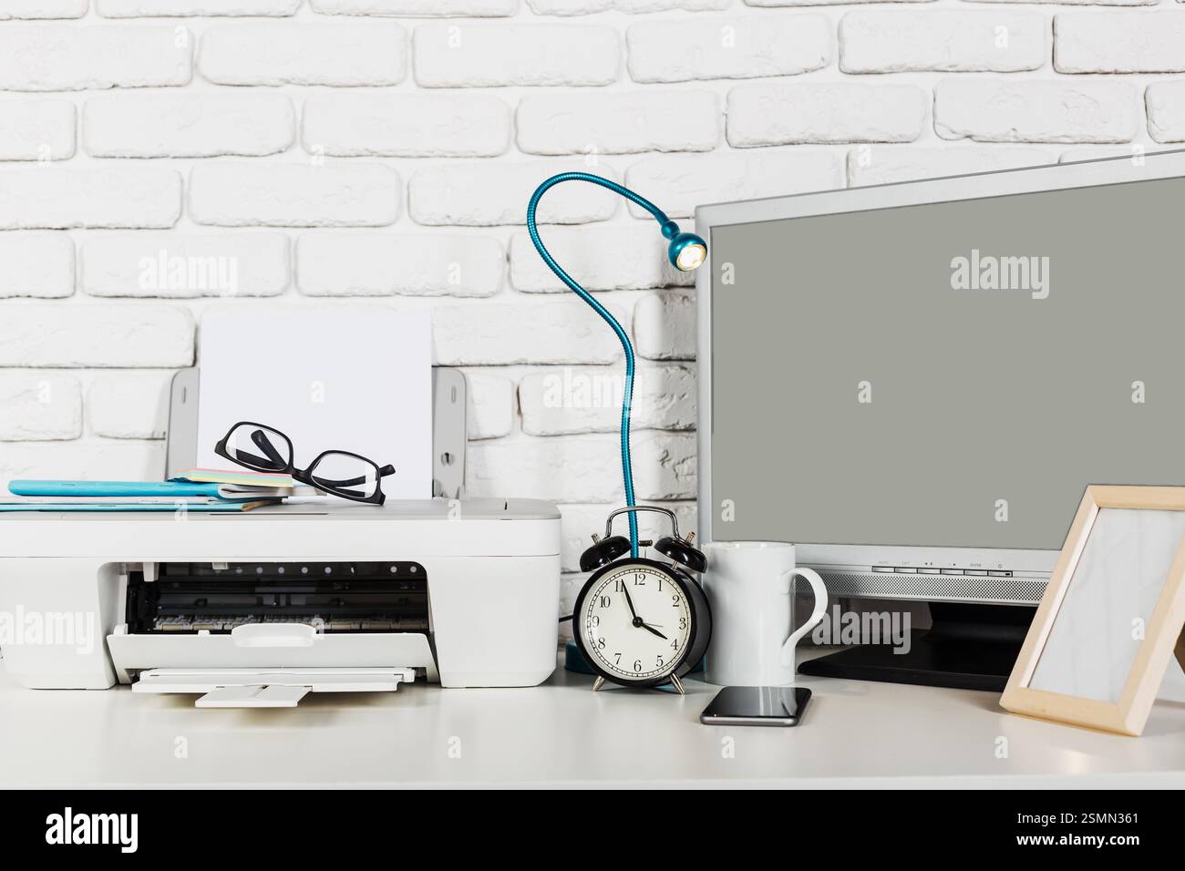 Desk workspace featuring a printer, clock, monitor, and office supplies ...