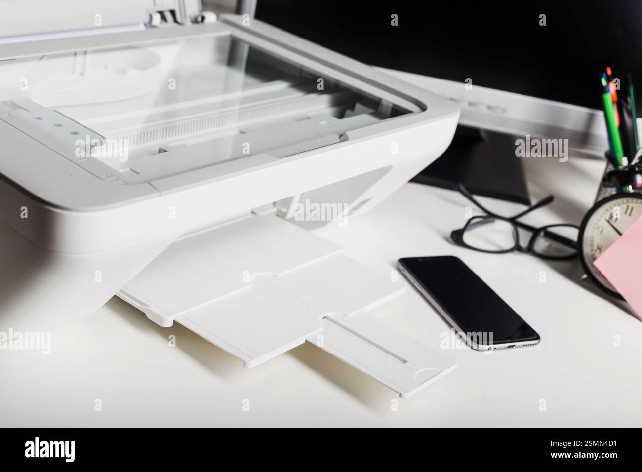 Office lighting highlights a modern printer beside a smartphone and a ...