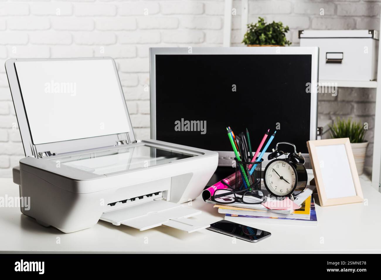 Desk clutter with printer, computer, and office supplies in a bright ...
