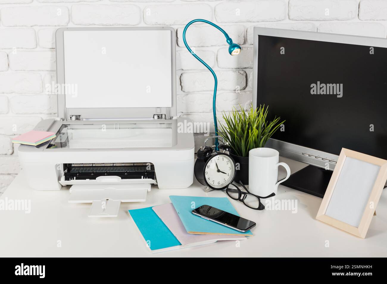 Desk setup featuring printer, clock, computer, and personal items in a ...