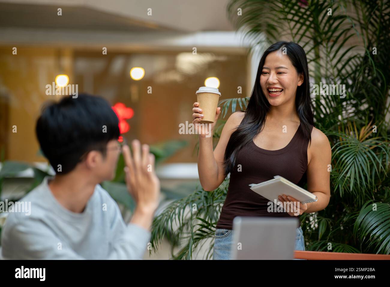 A cheerful, friendly Asian woman smiles and greets her friend at a ...