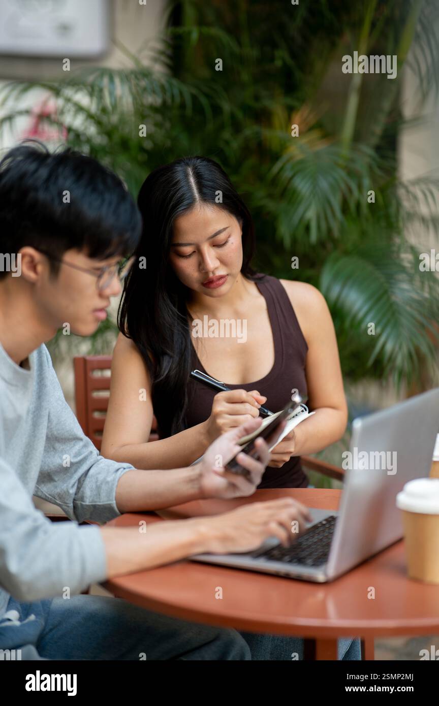 A beautiful, focused Asian woman attentively takes notes while ...
