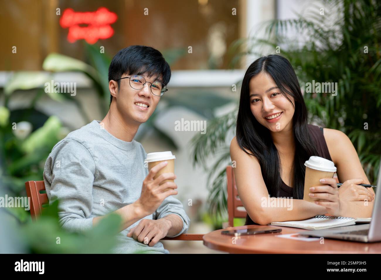 Two cheerful and positive Asian male and female friends are sitting at ...