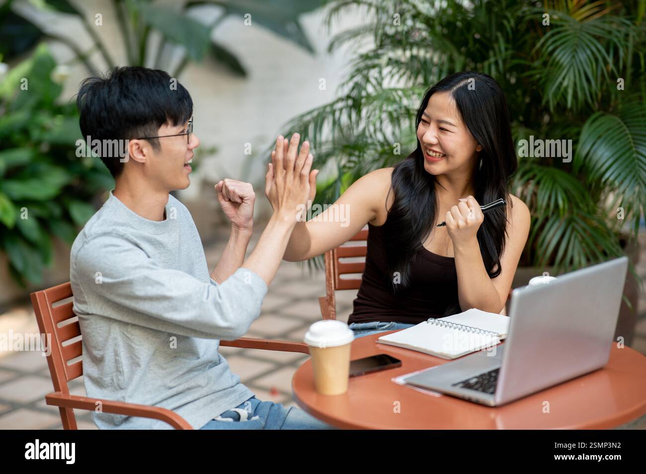 A cheerful, beautiful Asian woman gives a high five to her colleague ...