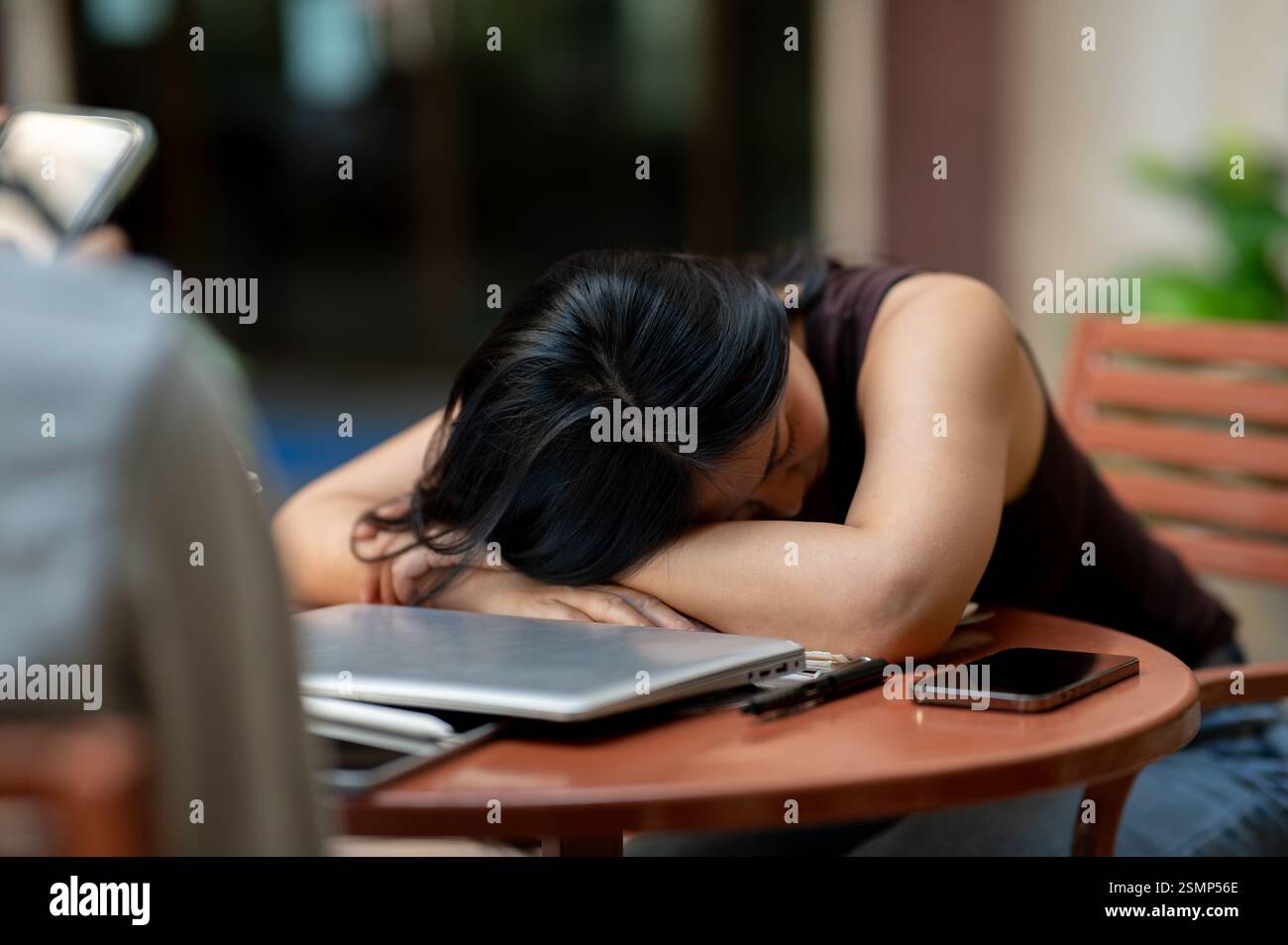 A tired, sleep-deprived Asian woman takes a nap at an outdoor table ...