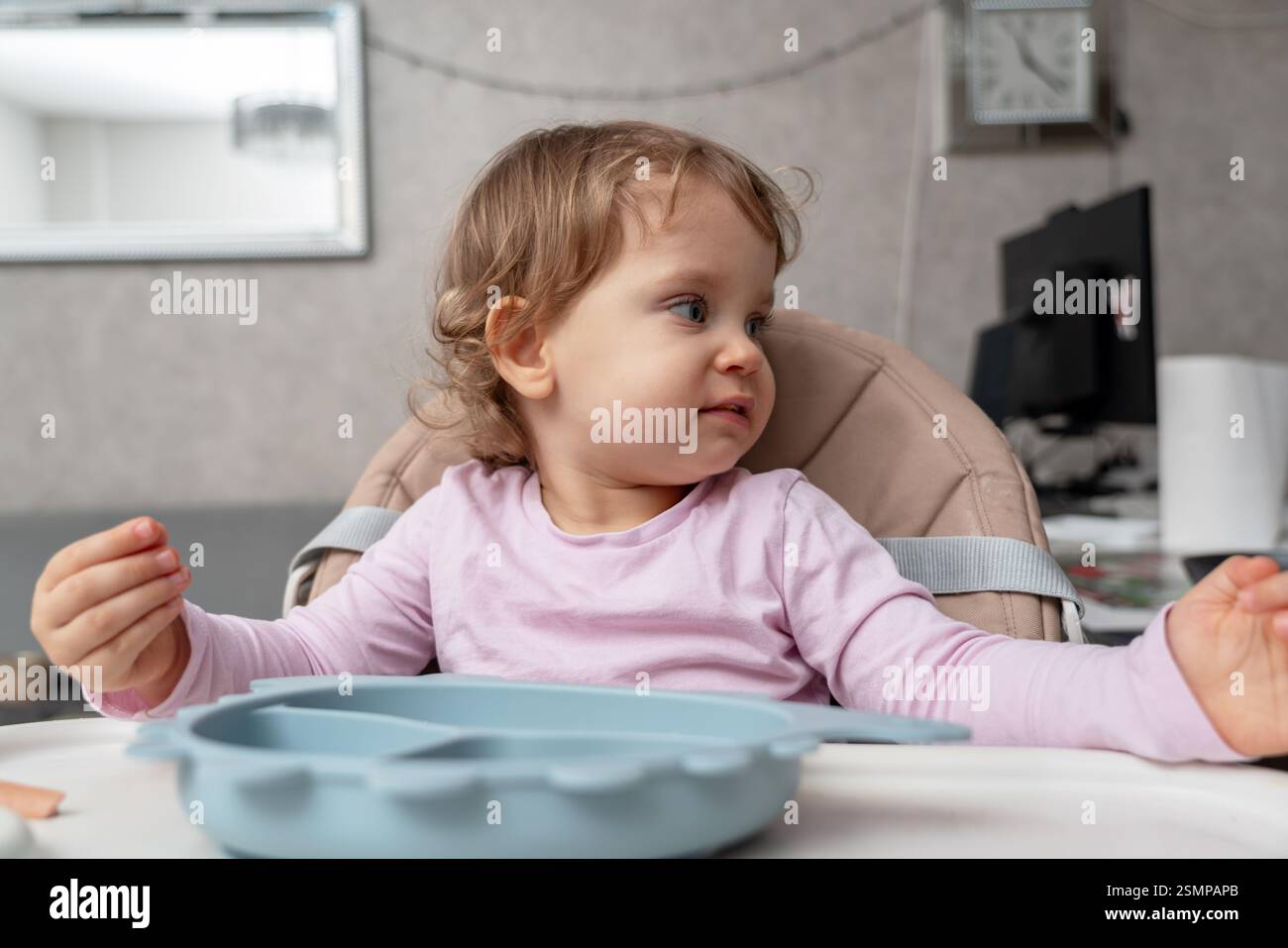 A curious toddler distracted during mealtime, observing surroundings ...