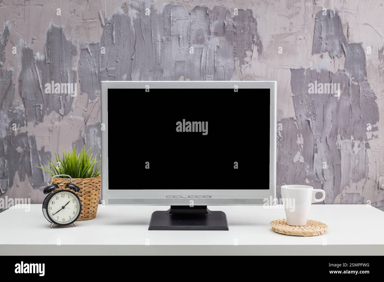 Desk setup featuring a blank computer monitor, clock, plant, and cup in ...