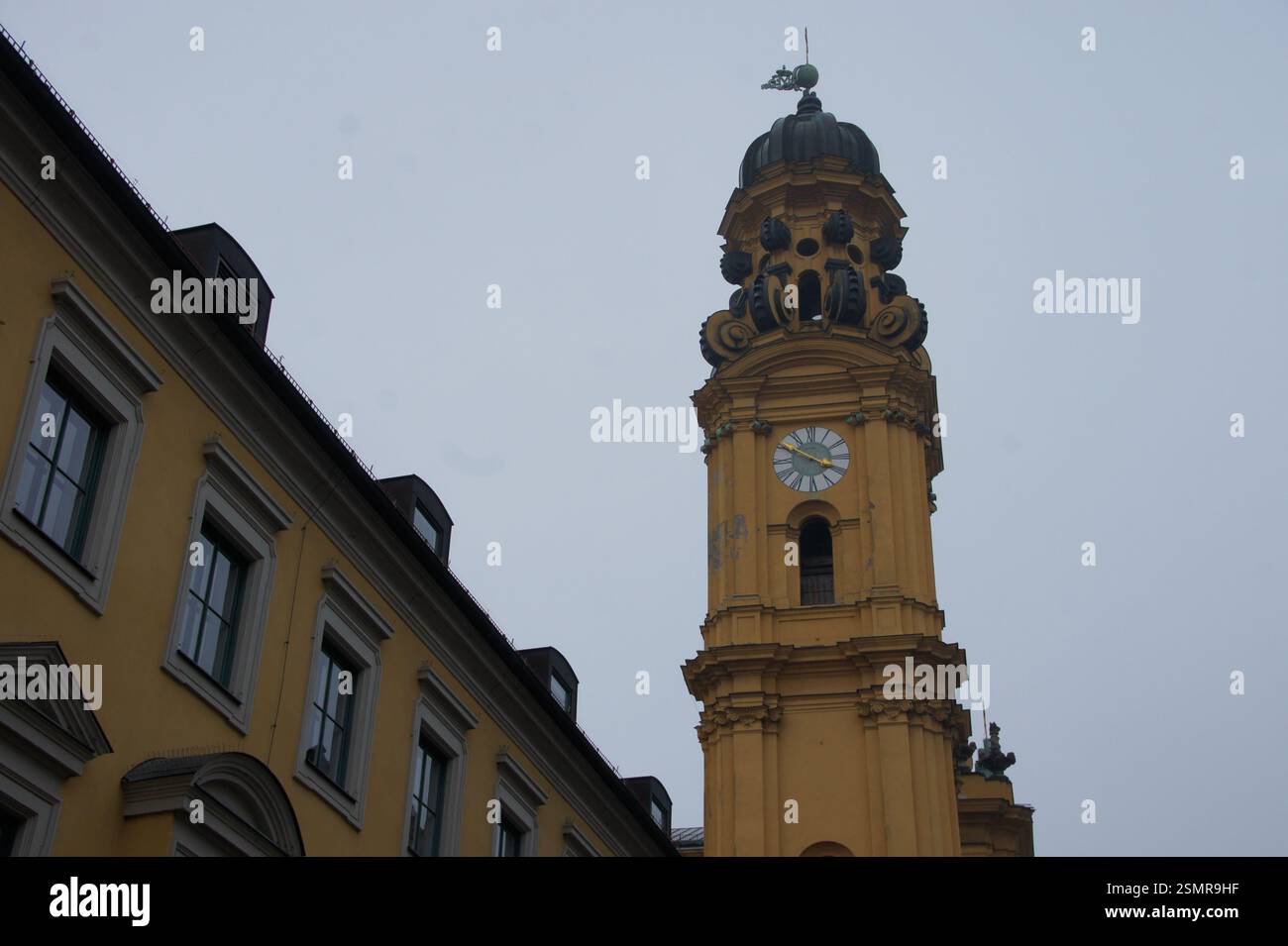 A tall clock tower with four faces stands next to a large gothic ...