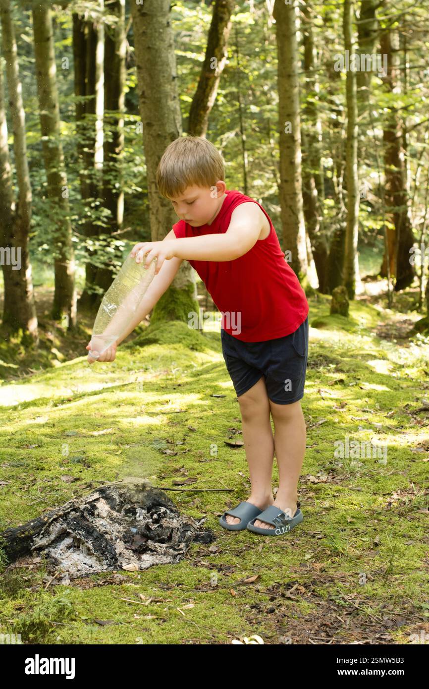A child in a red shirt and dark shorts stands in a mossy forest, gently ...