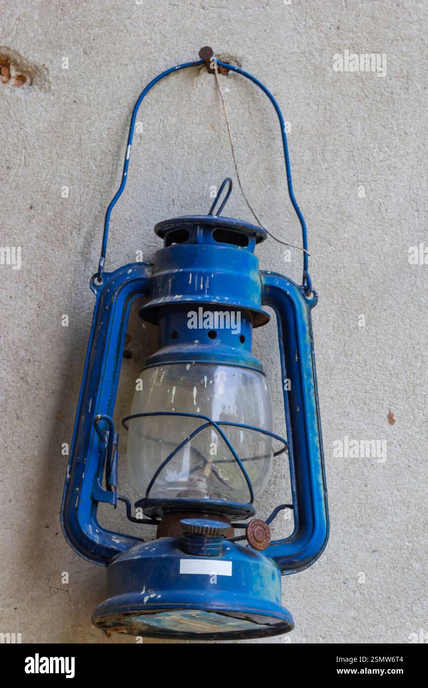 A rustic blue lantern is suspended from a wall in an aged building. The ...