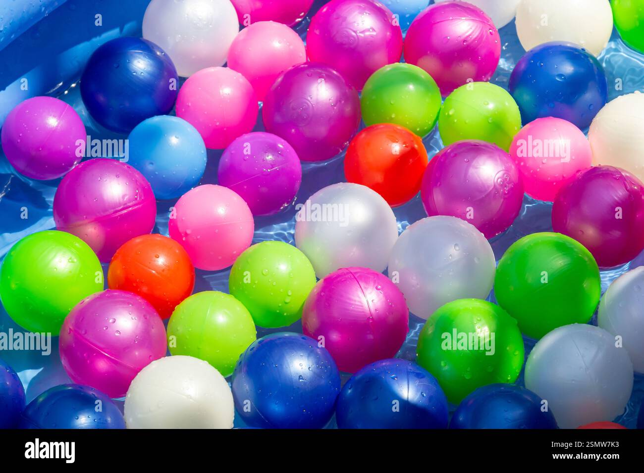 A variety of colorful plastic balls float in a clear blue pool, adding ...