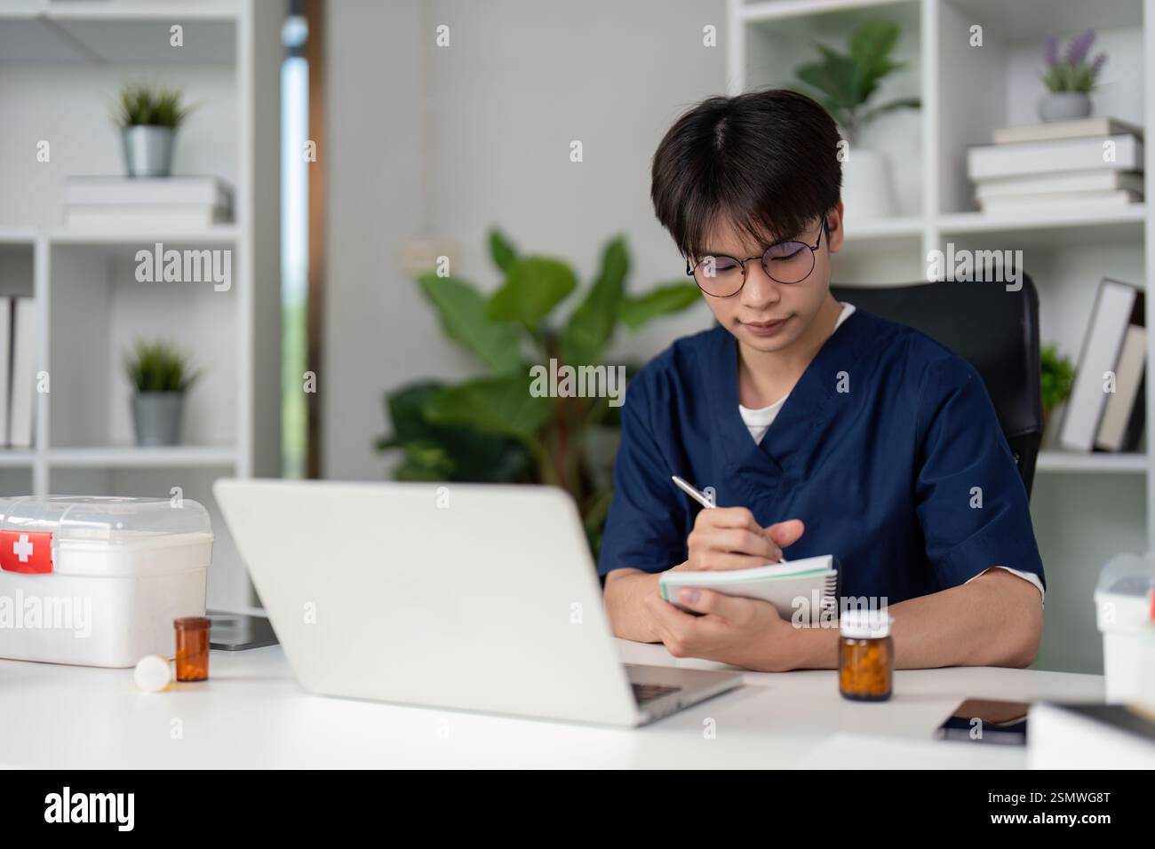 Medical student studying and taking notes at a desk with laptop and ...