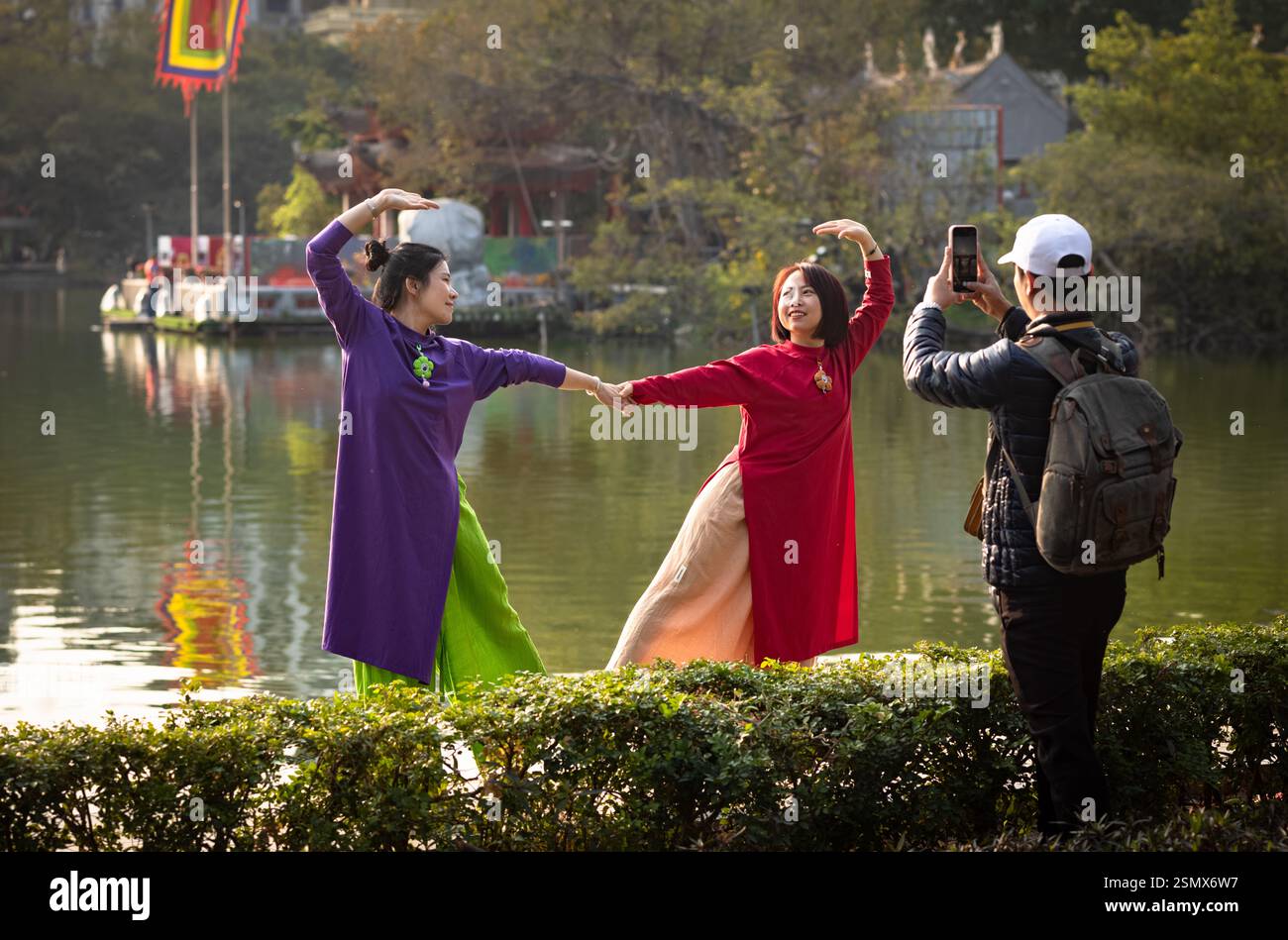 Two Vietnamese women dressed in traditional ao dai hold hands and form ...